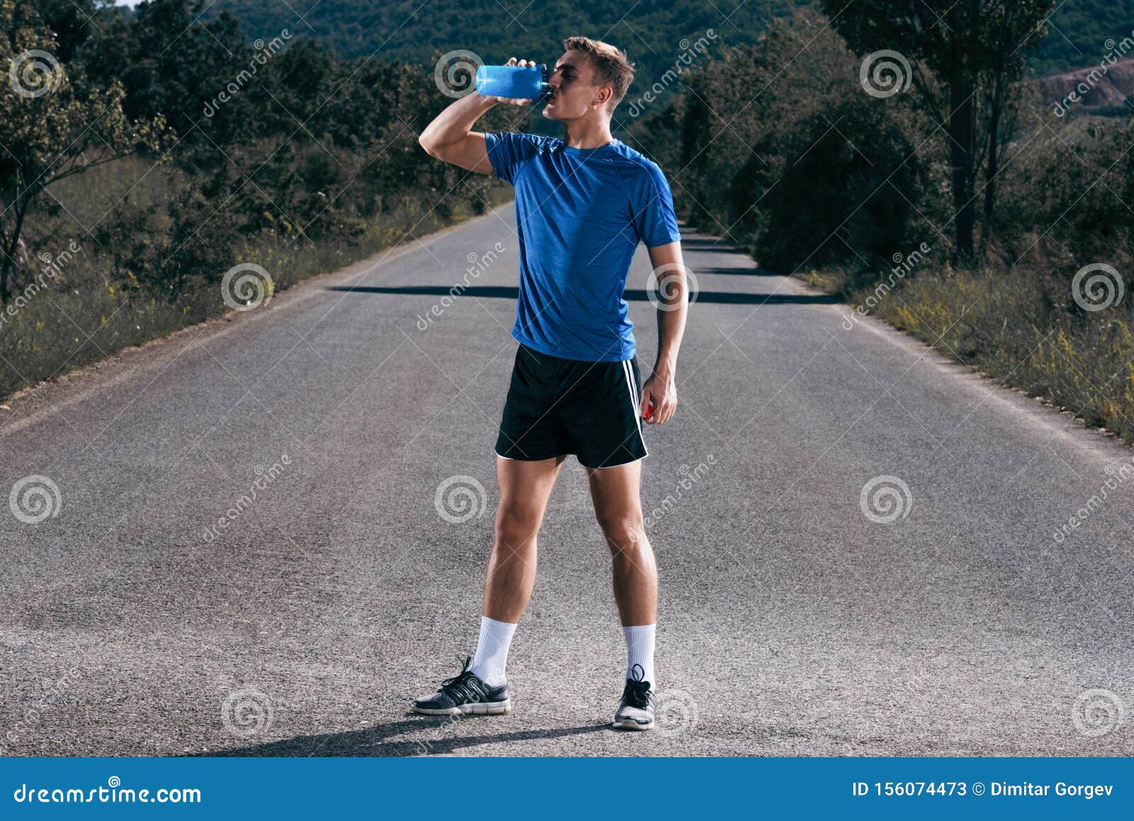 Fit Male Runner Drinking Water from a Water Bottle on an Empty Road in ...