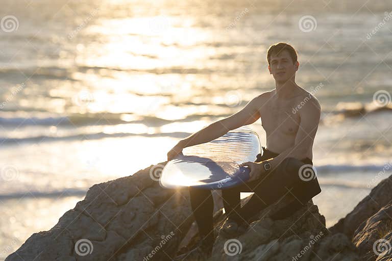 Fit Man With Naked Torso Sitting On The Rock At The Seashore Holding A