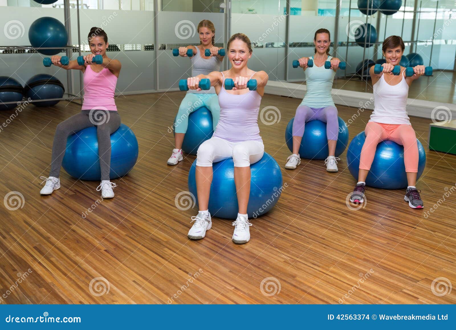 Fitness Class Holding Dumbbells on Exercise Balls in Studio Stock Photo ...