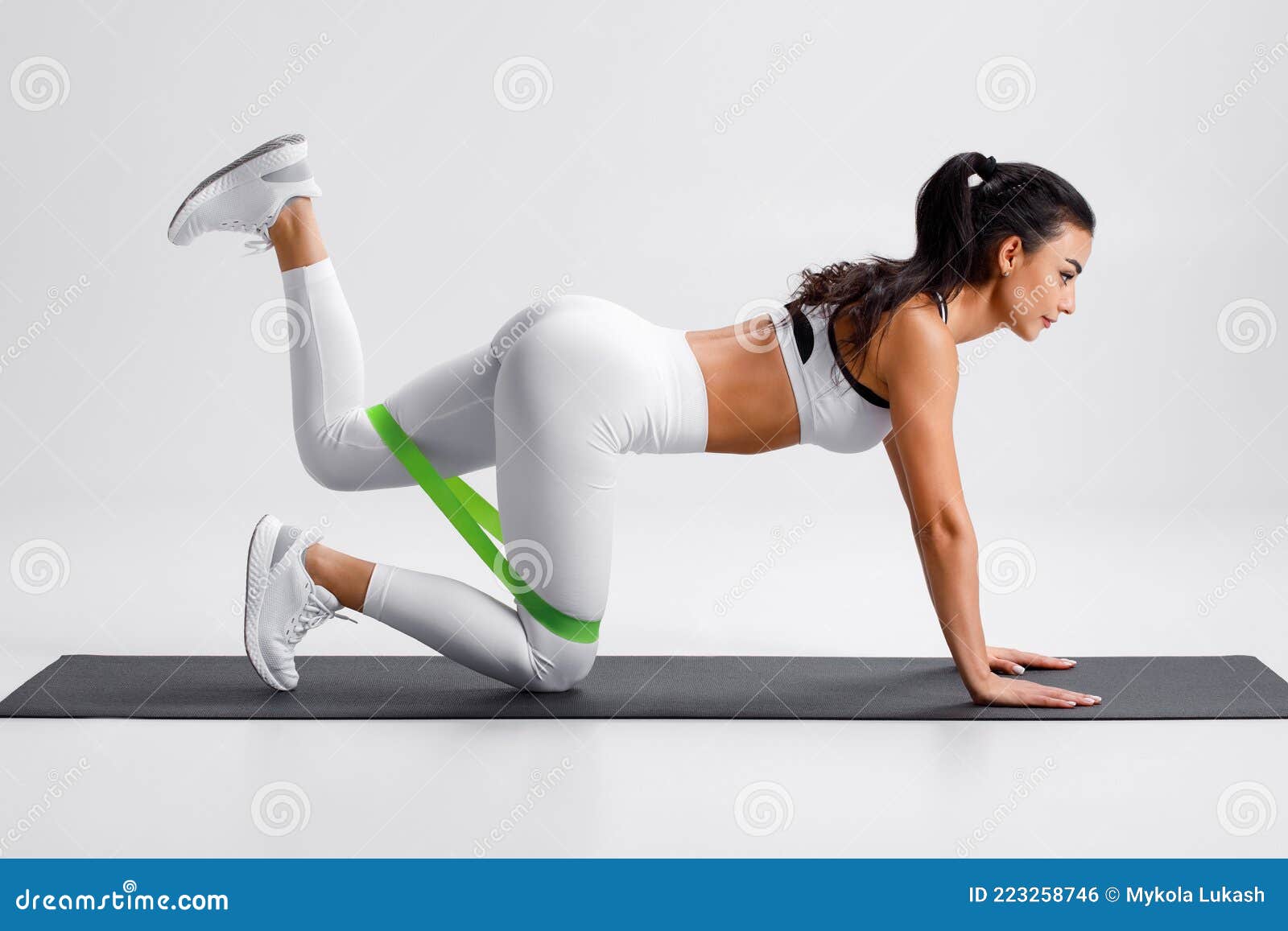 Fitness Woman Doing Kickback Exercise For Glutes With Resistance Band On Gray Background