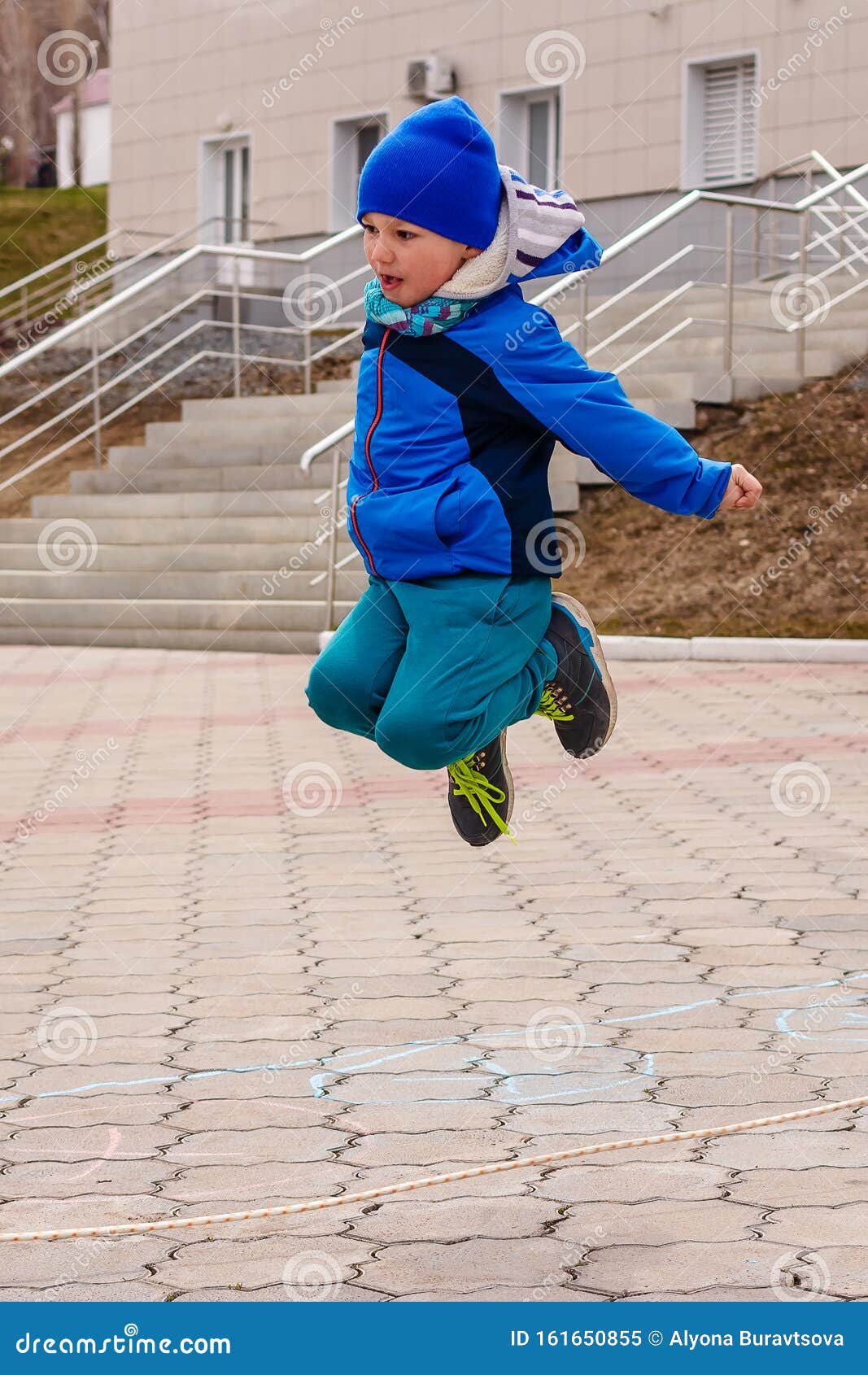 A Five-year-old Boy in a Blue Hat and Jacket Jumps Over a Rope High ...