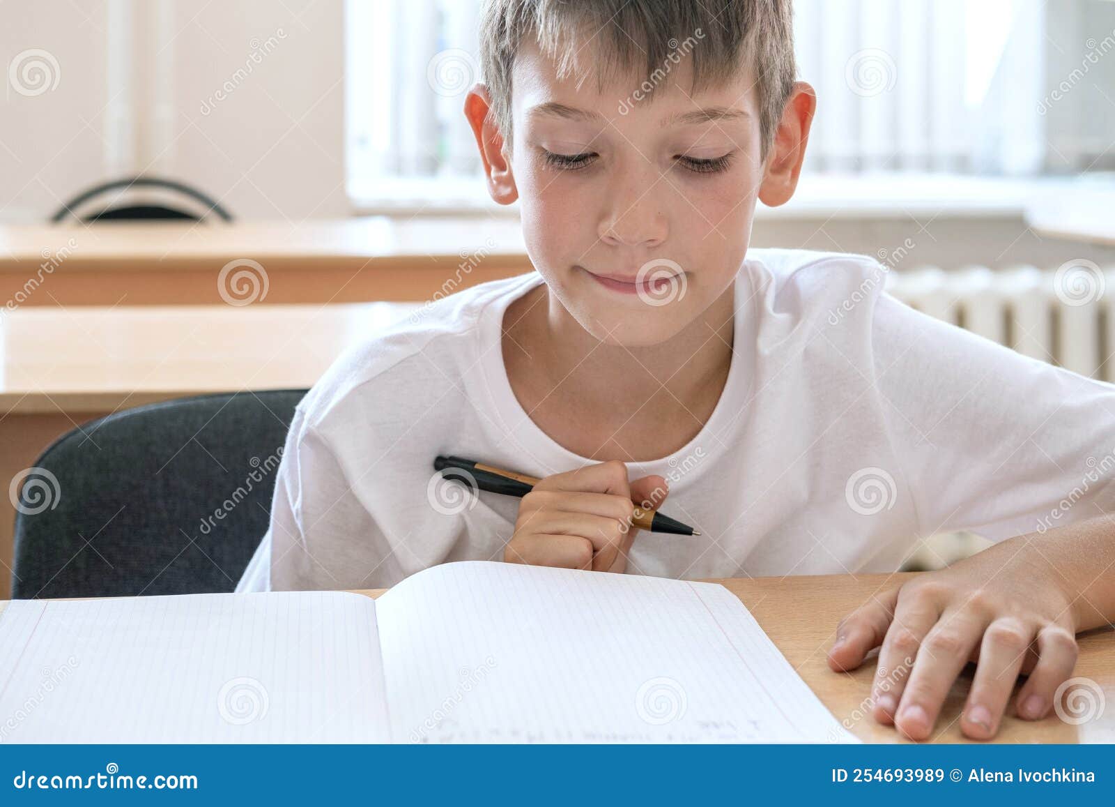 A Focused Boy Doing Homework, Writing Text in a Notebook at the Table ...