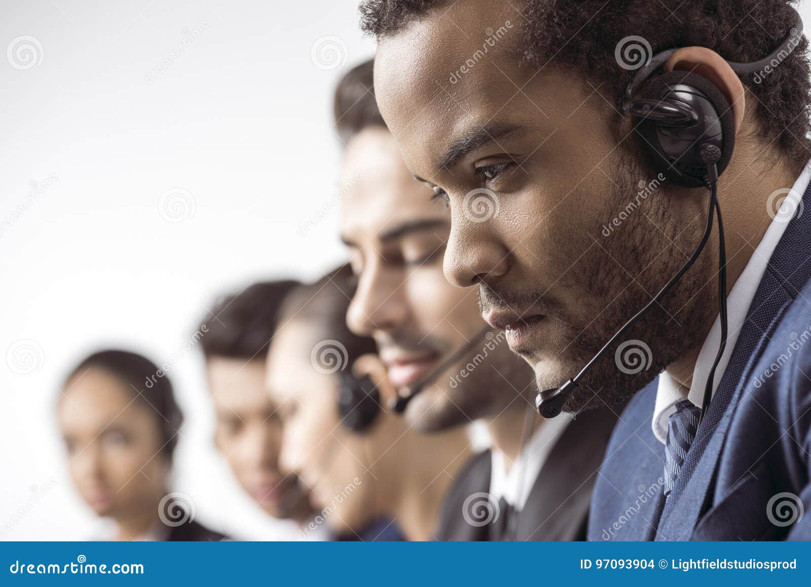 Focused Call Center Operator in Headset Working with Colleagues Behind ...