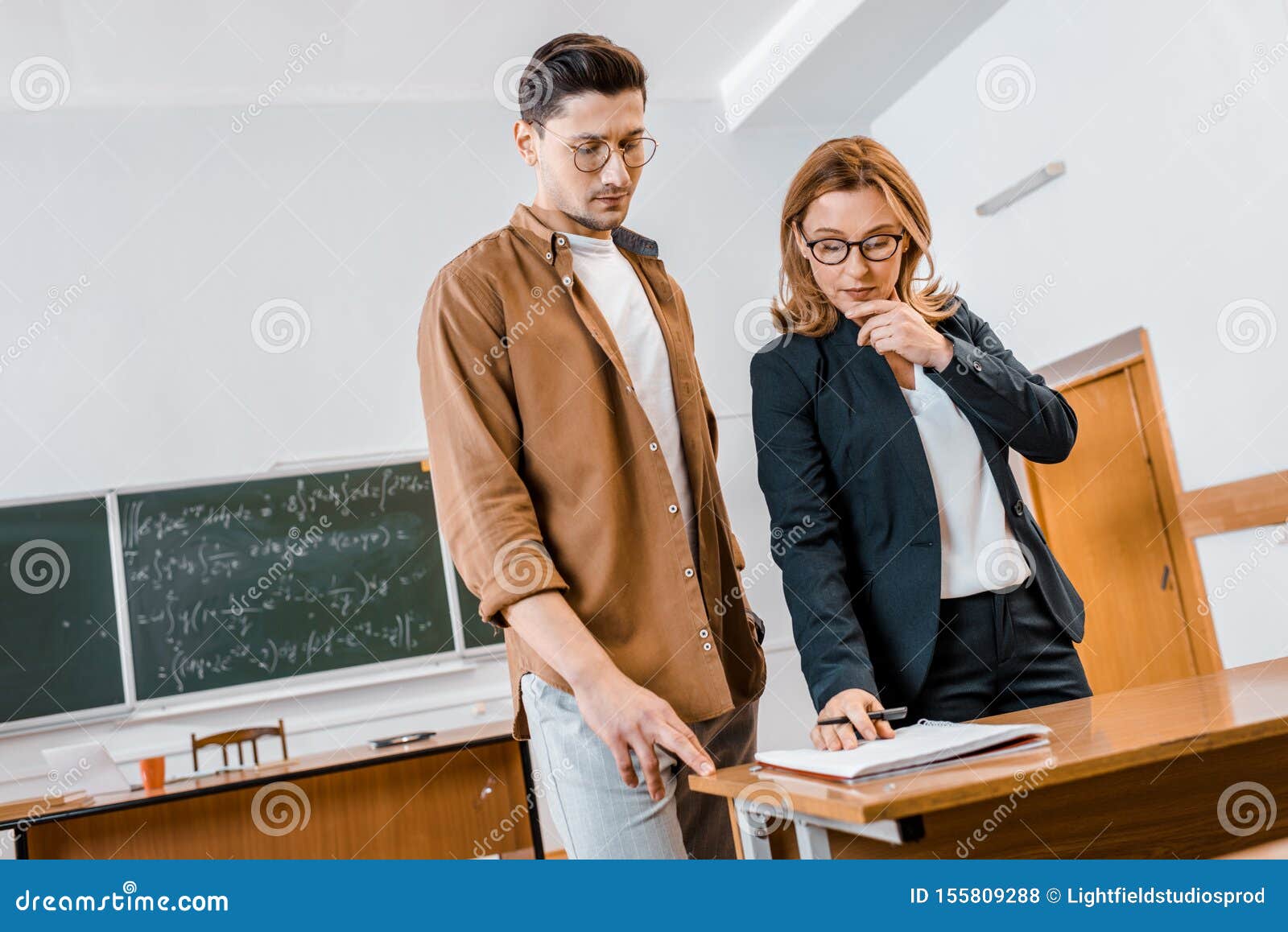 Focused Female Teacher Helping Male Student with Assignment during ...