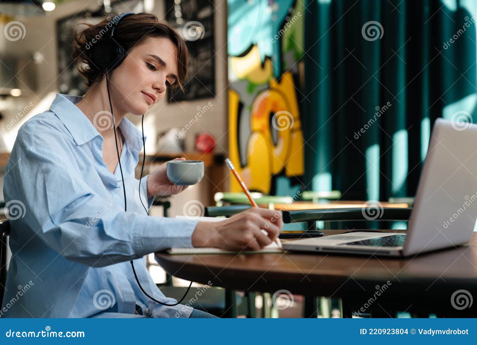 Focused Girl Writing Down Notes while Using Laptop and Headphones Stock ...