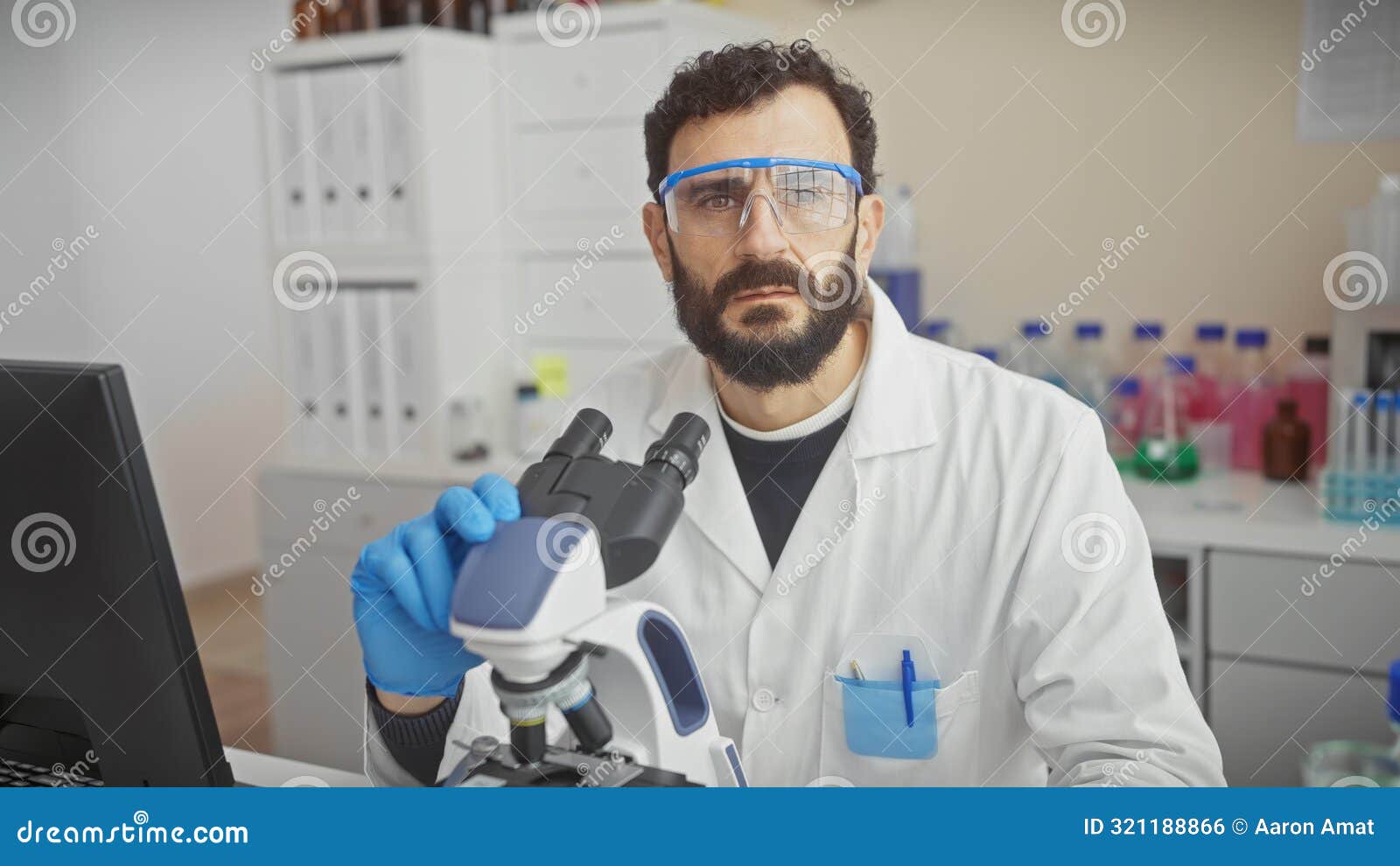 A Focused Man in a Lab Coat Using a Microscope in a Modern Laboratory ...