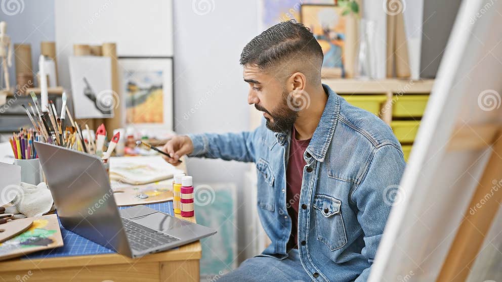 A Focused Man Painting in an Art Studio while Looking at a Laptop for ...