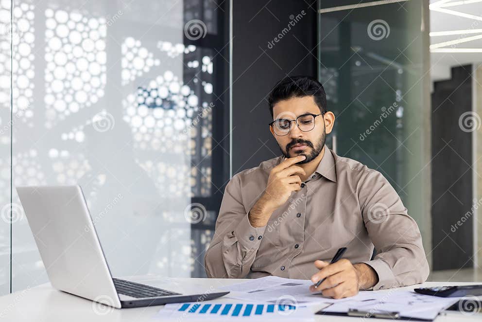 Focused Man Working on Laptop in Modern Office, Studying Paperwork and ...