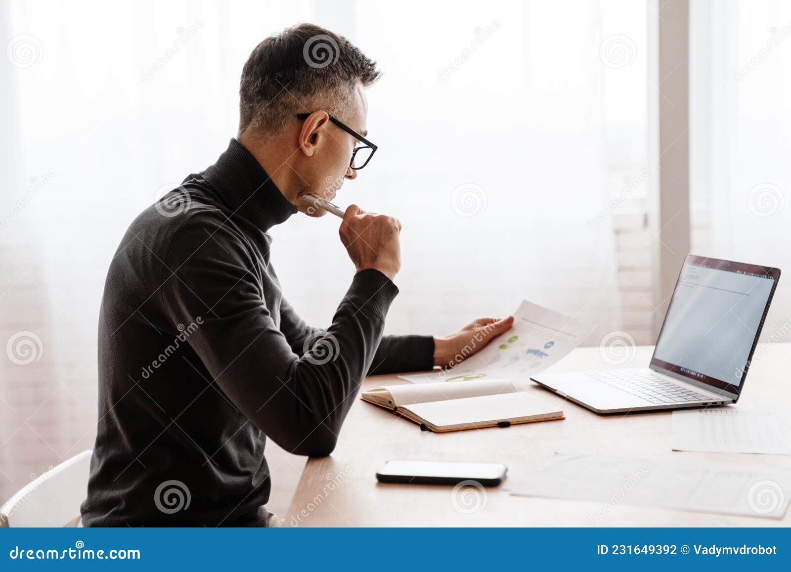 Focused Man Working with Laptop and Papers while Sitting at Table Stock ...