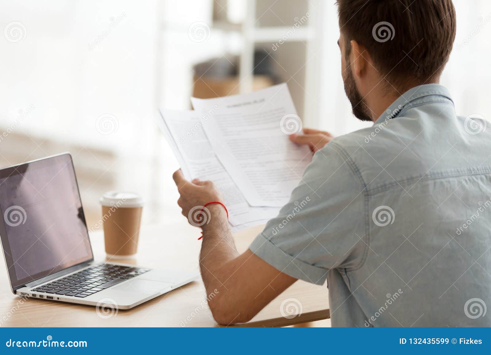 Focused Man Working at Laptop Reading Paperwork Documents Stock Image ...