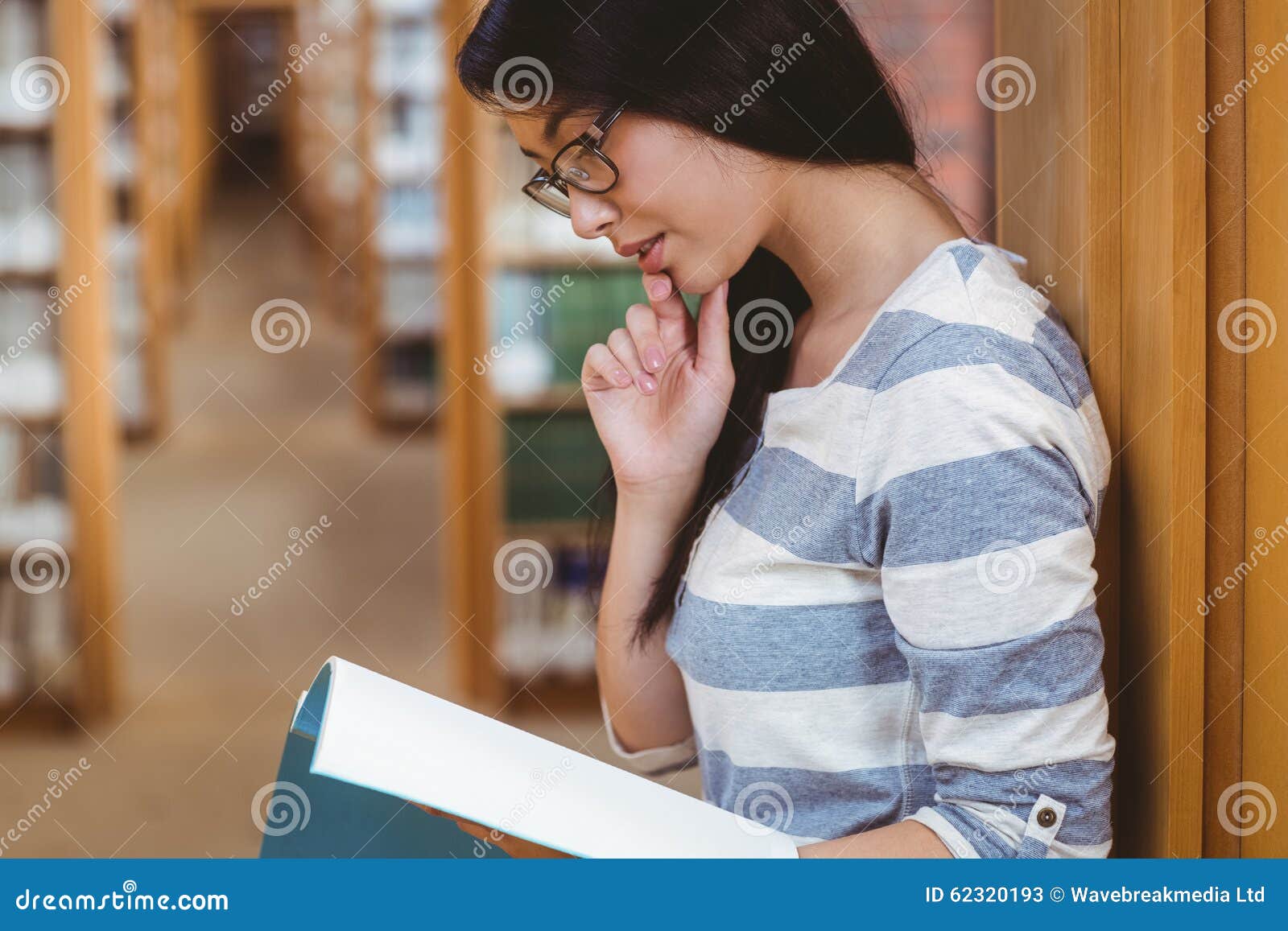 Focused Student Leaning Against Bookshelves and Reading a Book in ...
