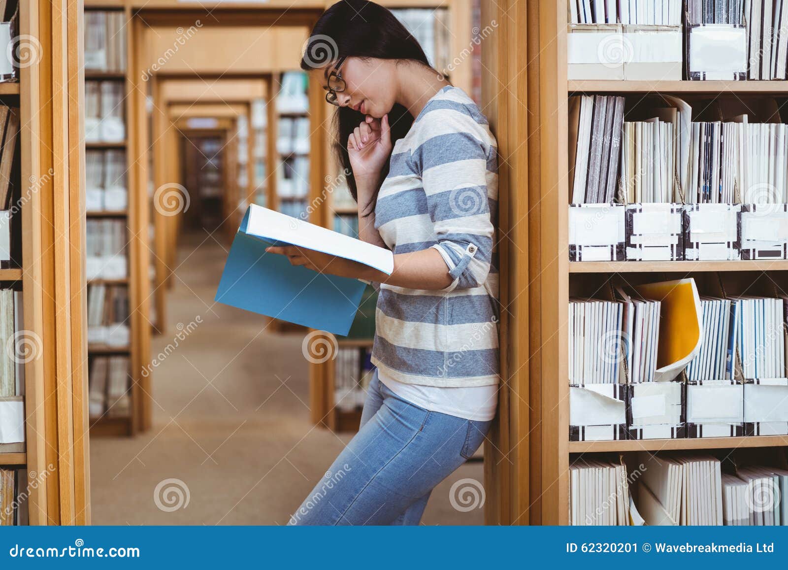 Focused Student Leaning Against Bookshelves and Reading a Book in ...