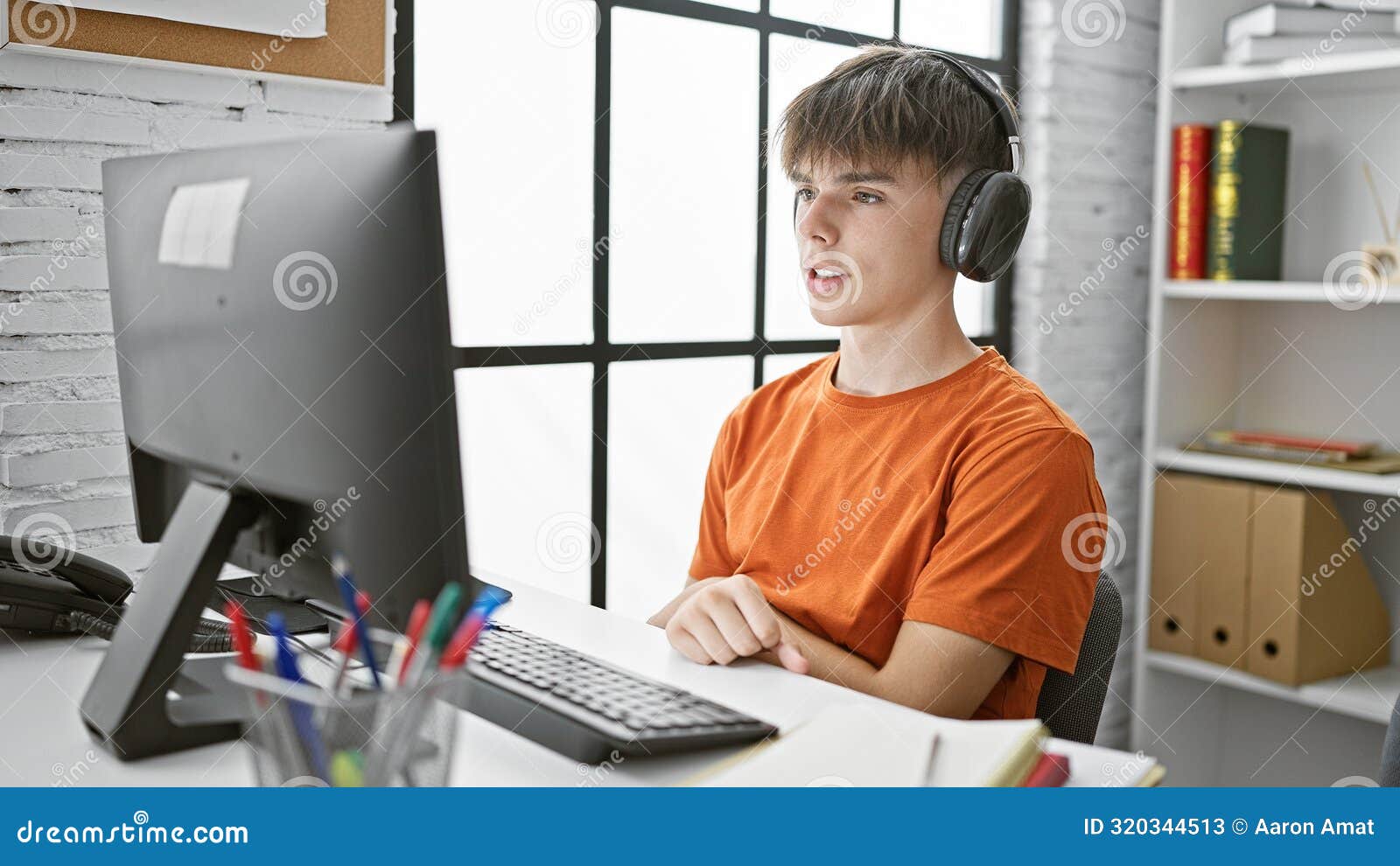 A Focused Teen Boy in a Classroom with Headphones Using a Computer ...