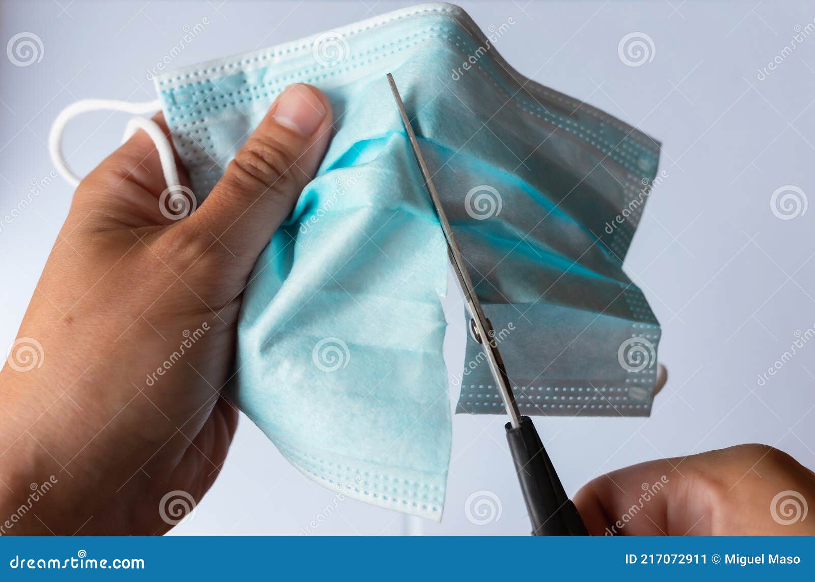 In the Foreground, Someone Cuts a Surgical Mask in Half with Scissors ...