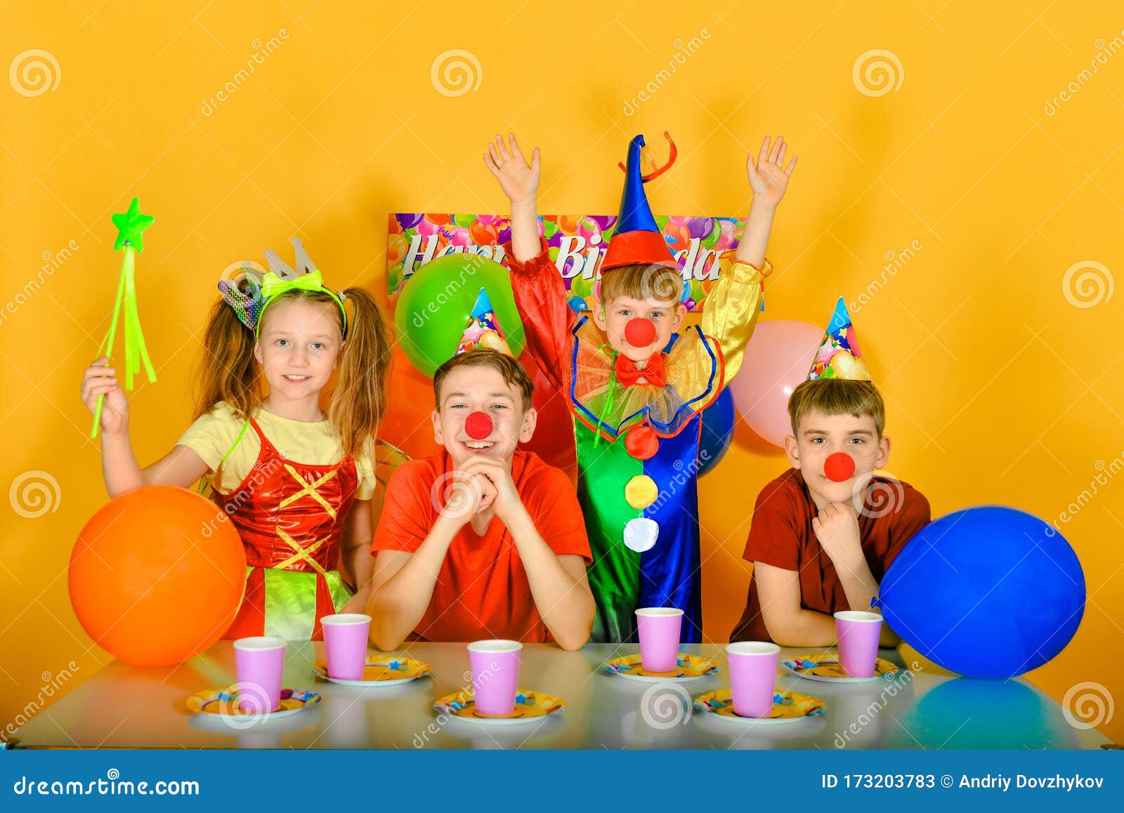 Four Children with a Clown at the Festive Table, Raise Their Hands Up ...