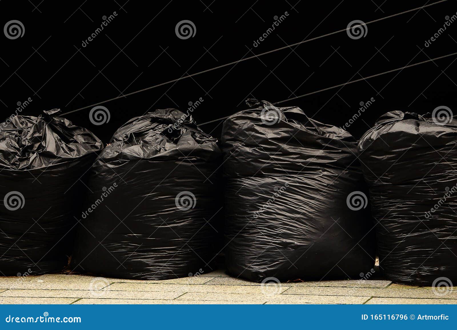 Four Filled Black Garbage Bags Standing Along a Black Wall Stock Photo ...