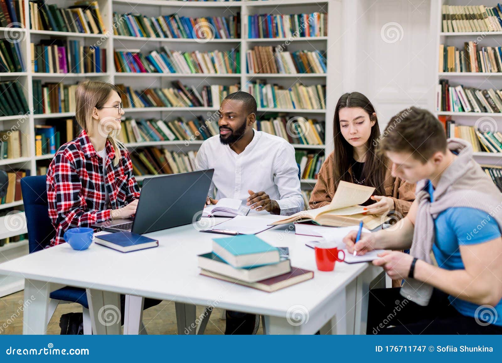 Four Multiracial Happy Students Sitting at Table in Library while ...