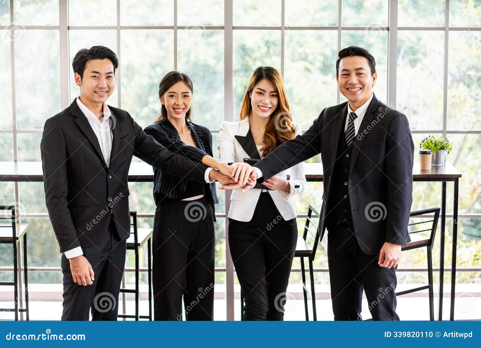 Four Professionals in Formal Attire Join Hands in a Modern Office ...