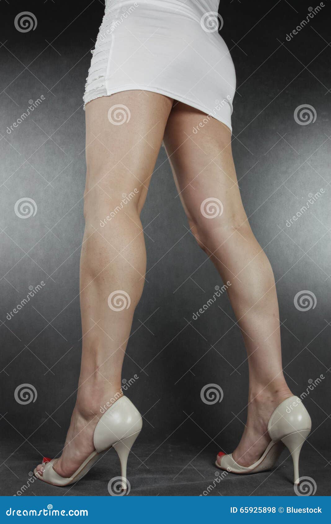 Frauenbeine Und Füße Die Kleid Und Fersen über Grauem Backgrou Tragen