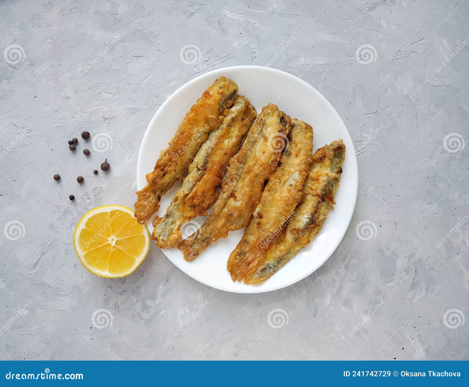 Fried Capelin Fish in a White Plate with Lemon and Pepper on a Gray ...