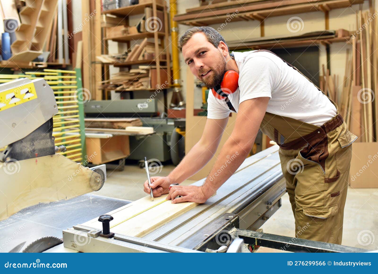 Friendly Carpenter with Ear Protectors and Working Clothes Working on a ...