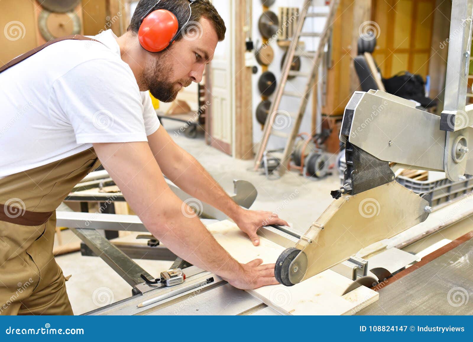 Friendly Carpenter with Ear Protectors and Working Clothes Working on a ...
