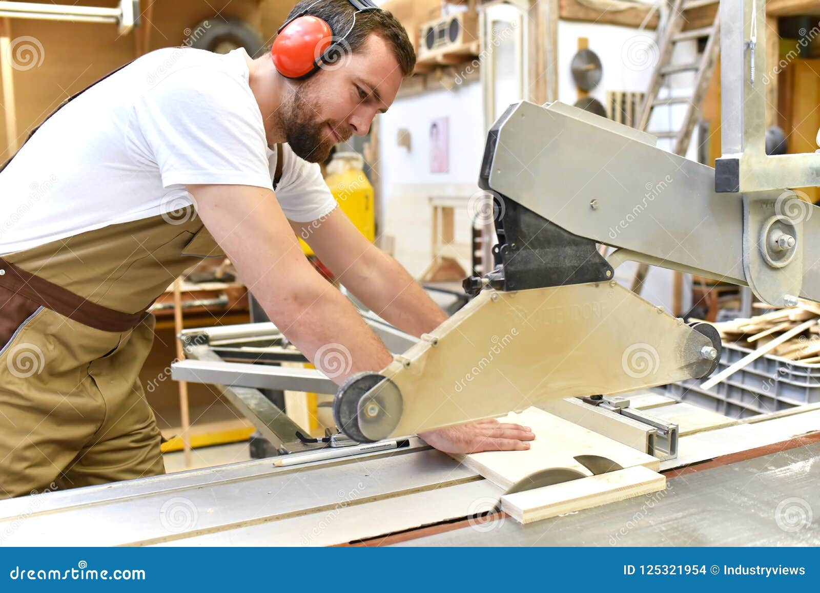 Friendly Carpenter with Ear Protectors and Working Clothes Working on a ...