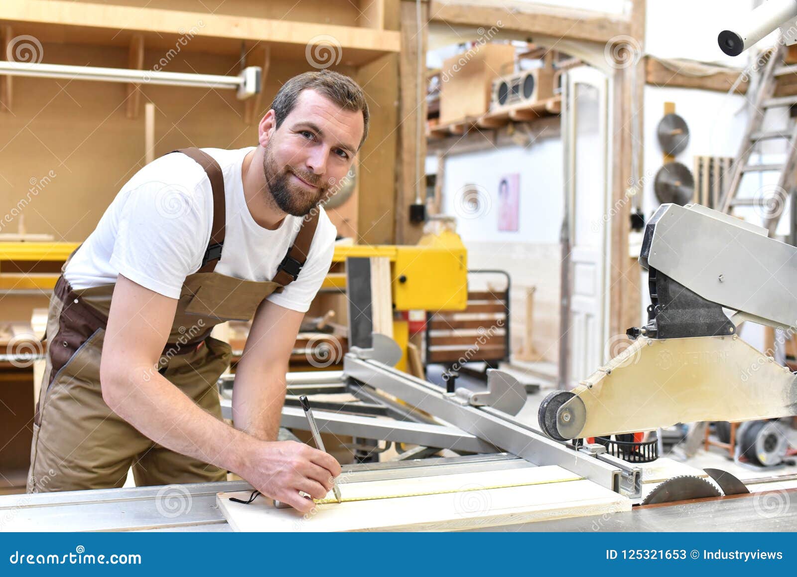 Friendly Carpenter with Ear Protectors and Working Clothes Working on a ...
