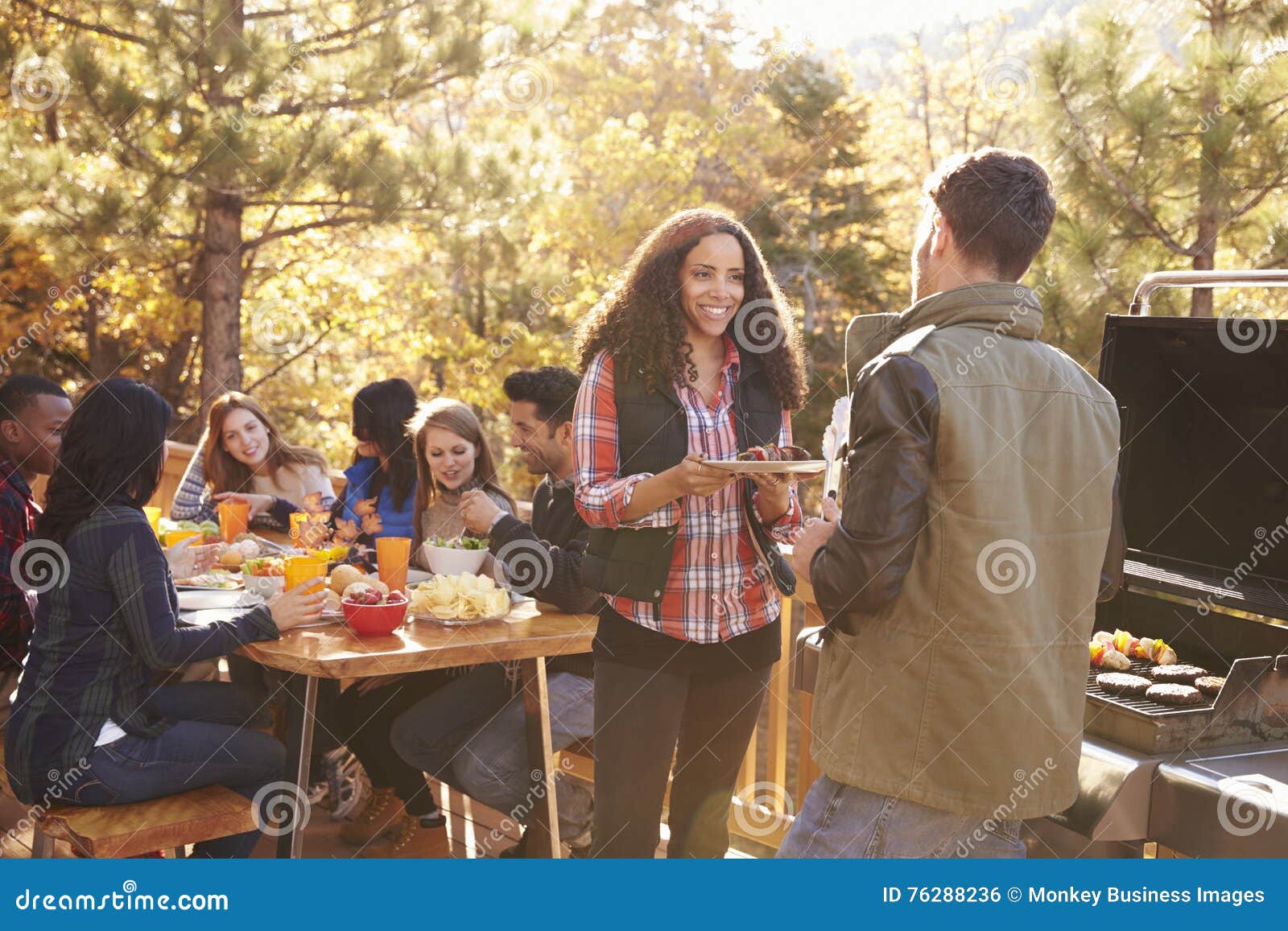 Friends Eat at Table and Two Talk by the Grill at a Barbecue Stock ...