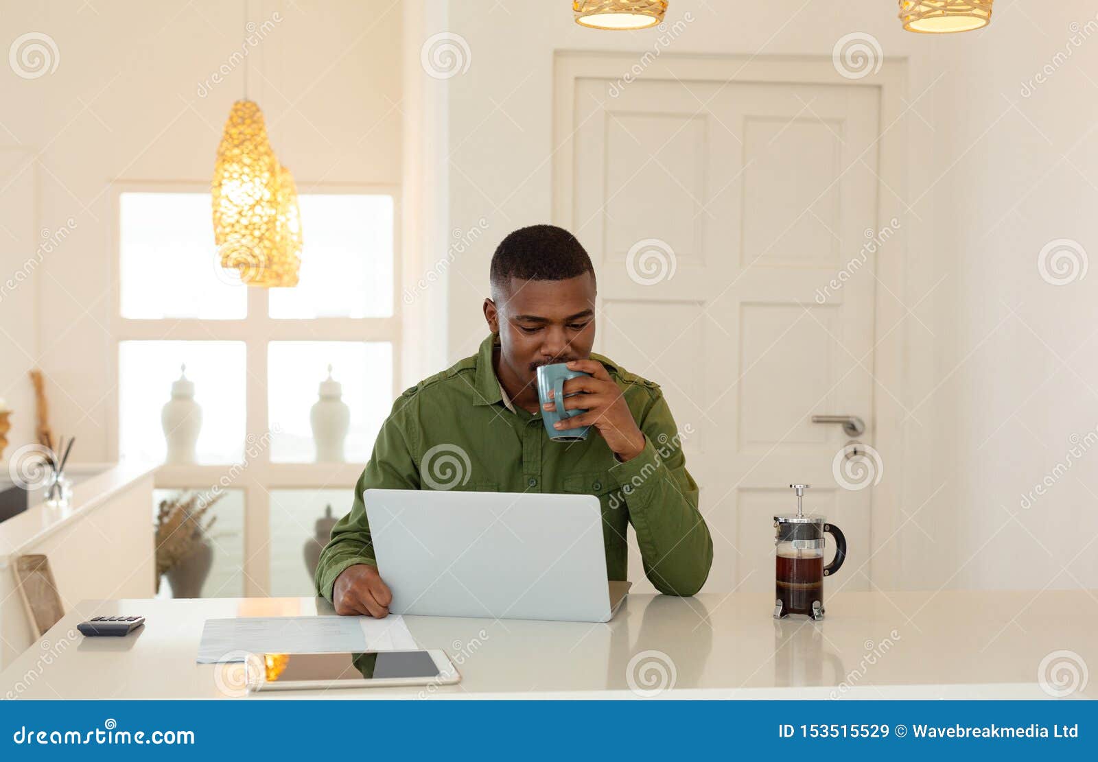 Man Drinking Coffee while Working on Laptop at Dining Table in Kitchen ...