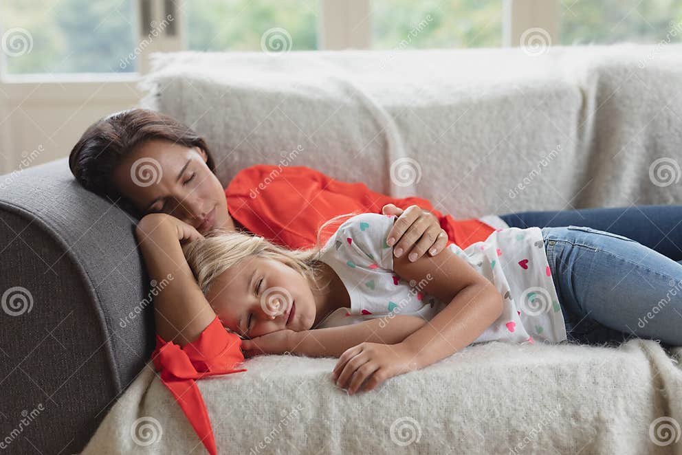 Mother And Daughter Sleeping Together On A Sofa In Living Room Stock