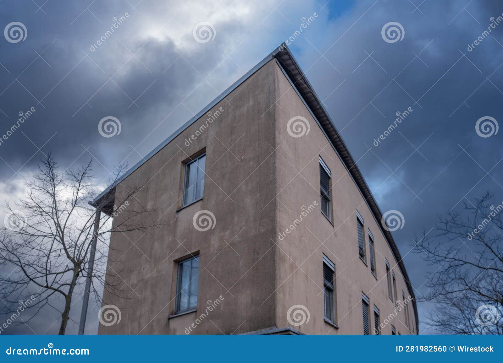 The Front Side of a Building with Trees and Dark Clouds Stock Photo ...