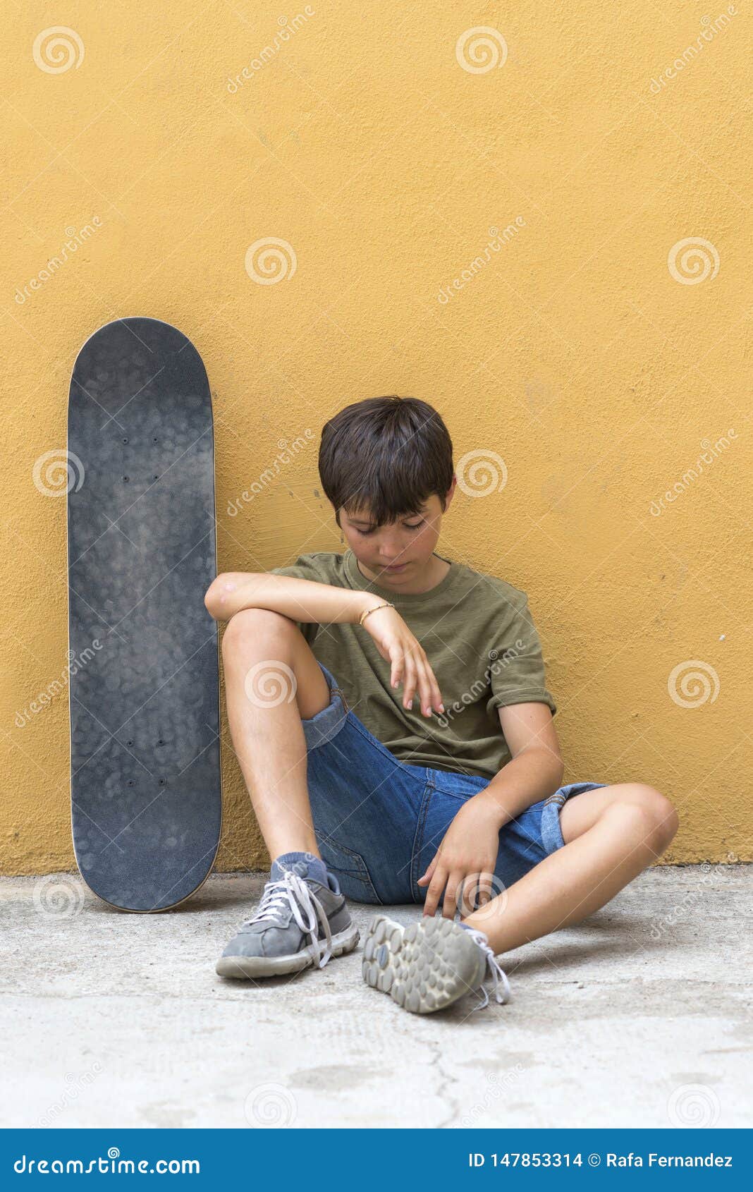 Front View of a Young Boy Sitting on Ground Leaning on a Yellow Wall ...