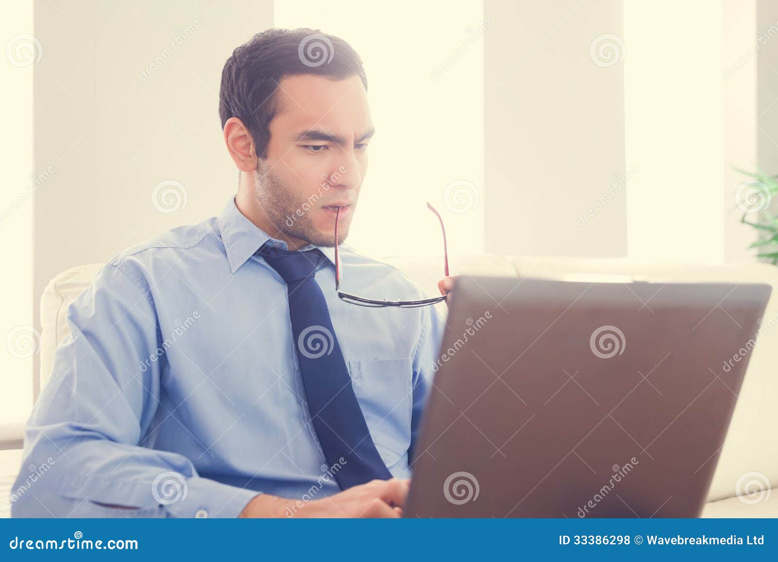 Frowning Man Biting His Eyeglasses and Using a Laptop Stock Photo ...