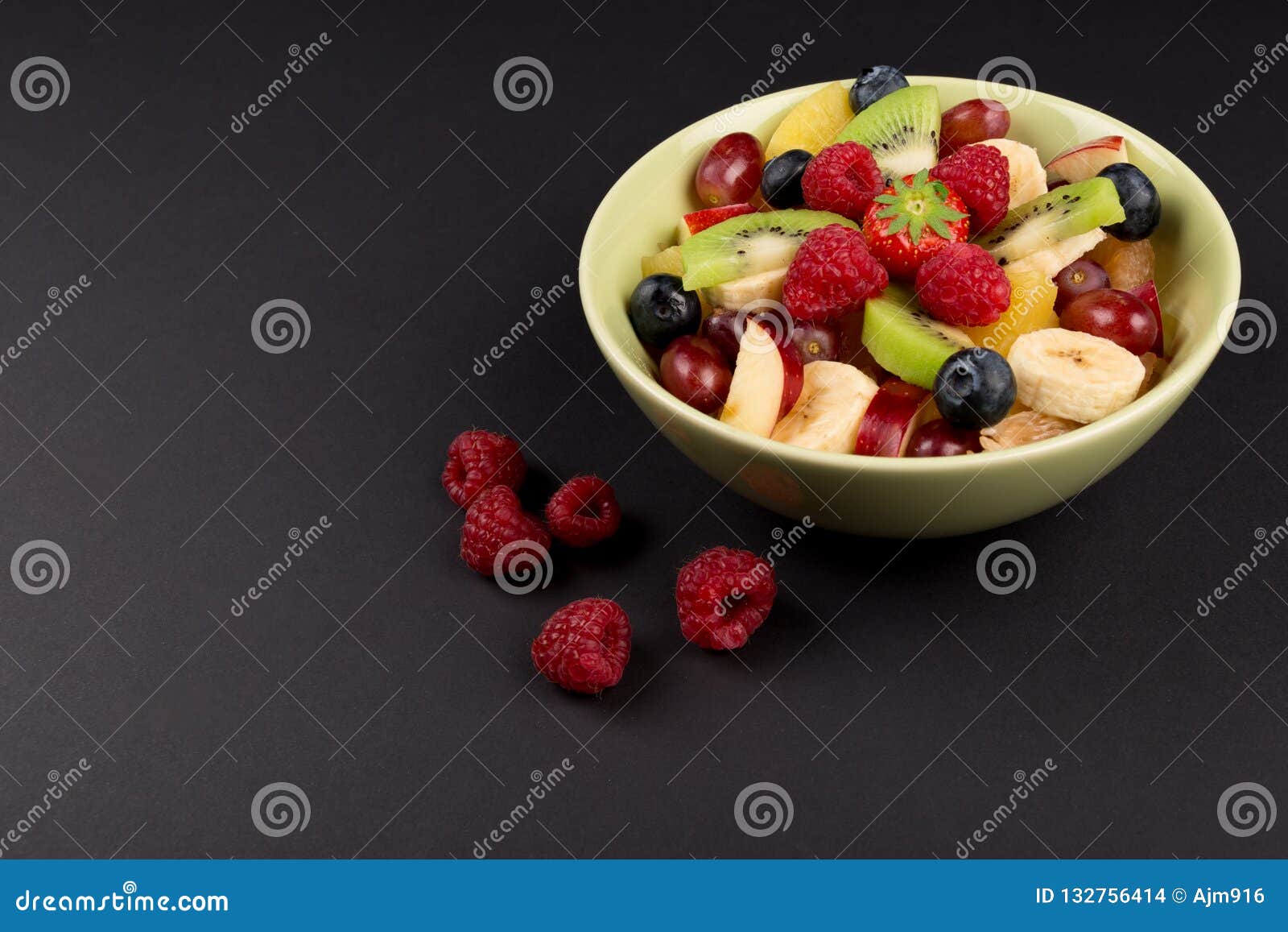 Fruit Salad in Green Bowl and Raspberries on Black Table, Side View ...