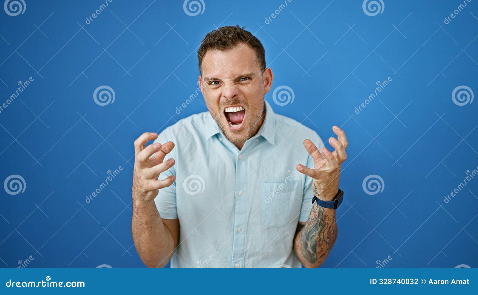 A Frustrated Young Man with a Beard Expressing Anger in Front of a Blue ...