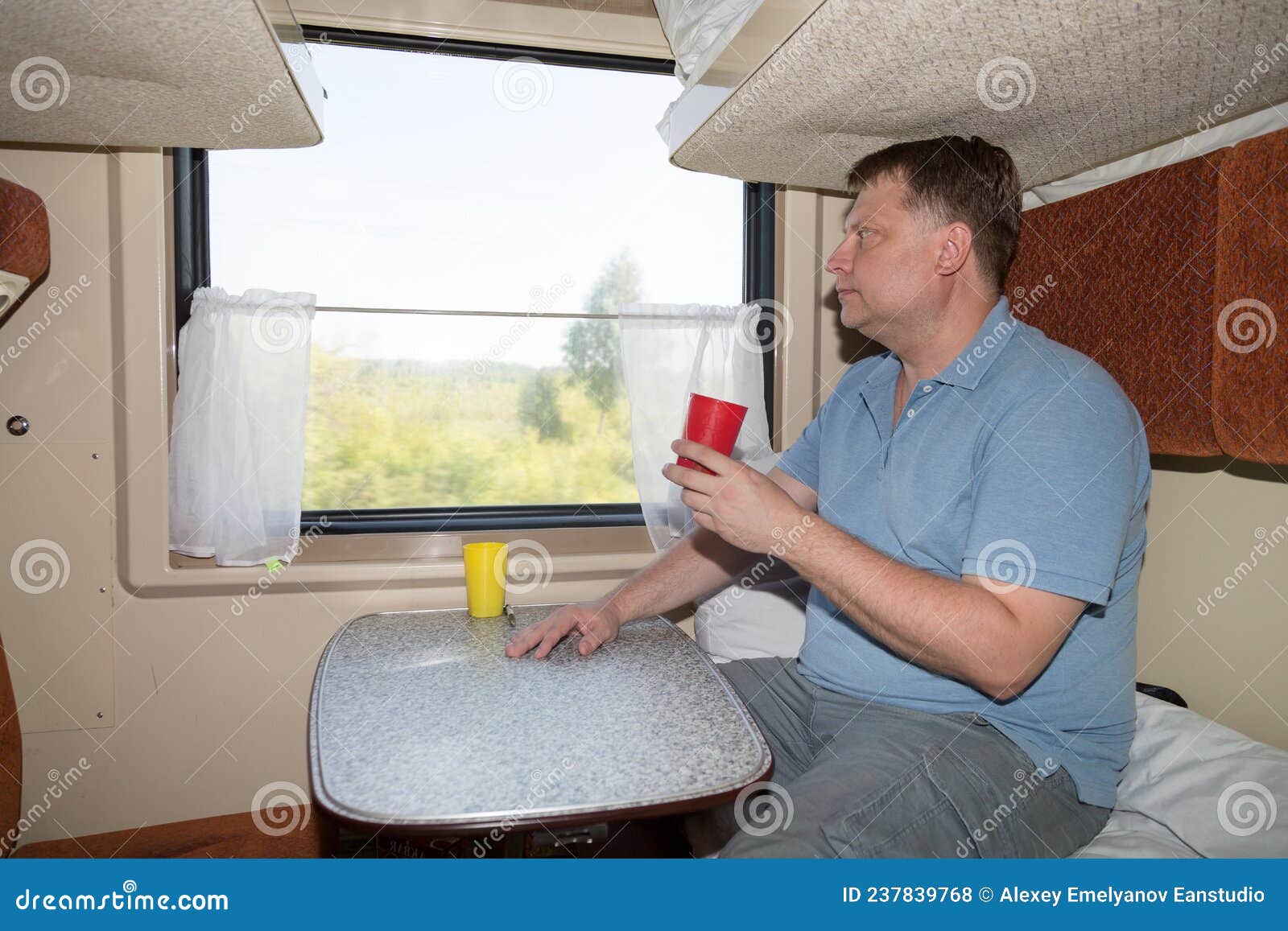 A Full Grown Man in a Train Compartment is Sitting at a Table with a ...
