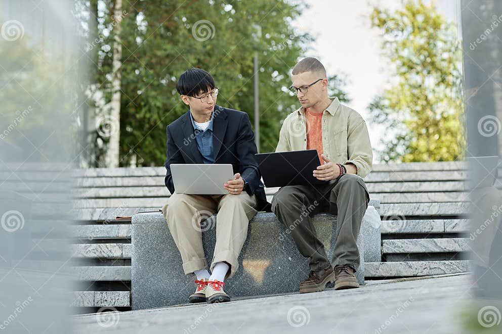 Two Businessmen Using Laptops To Work Sitting on Bench Outdoors Stock ...