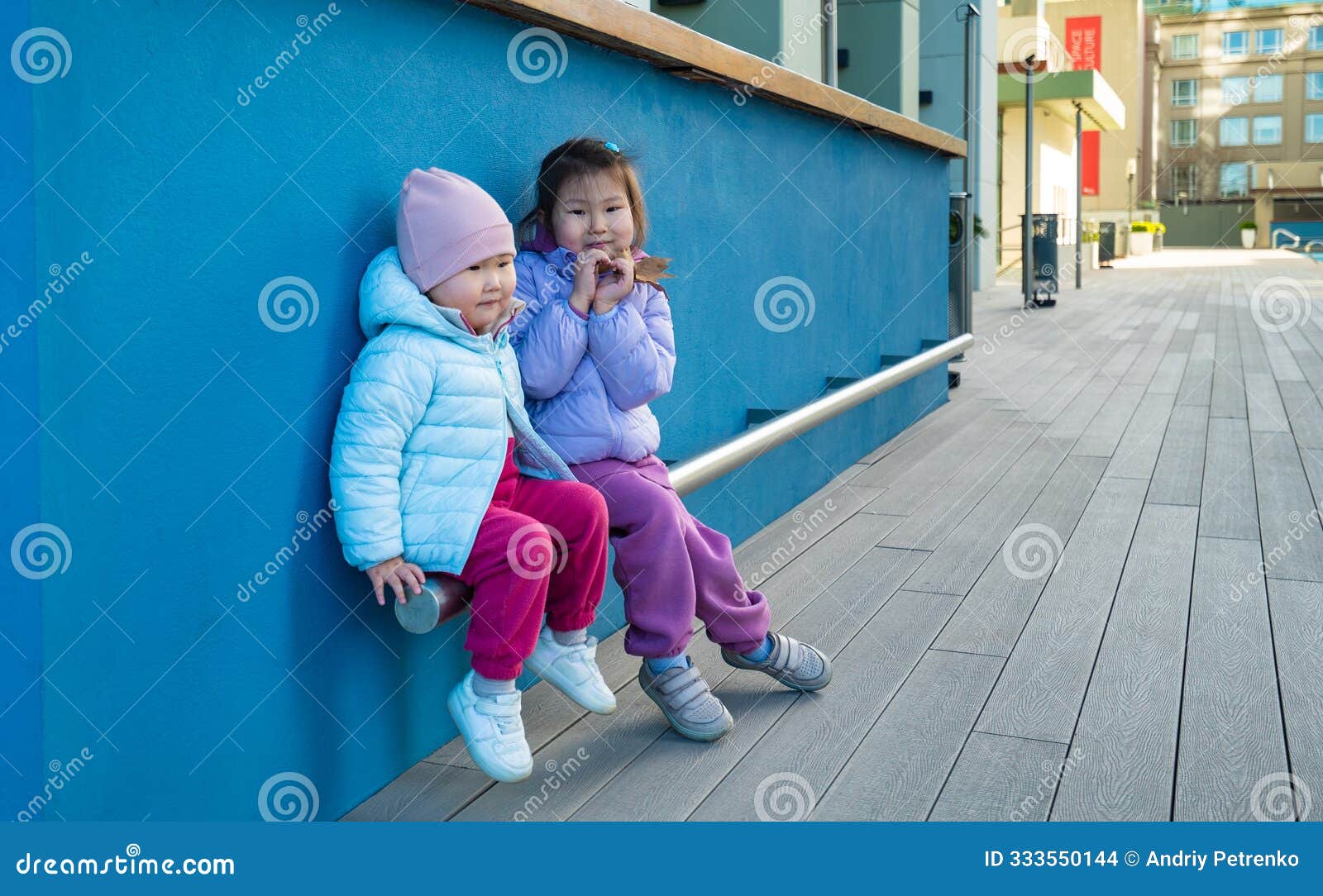 Two Young Children are Sitting on a Ledge, One Wearing a Pink Jacket ...