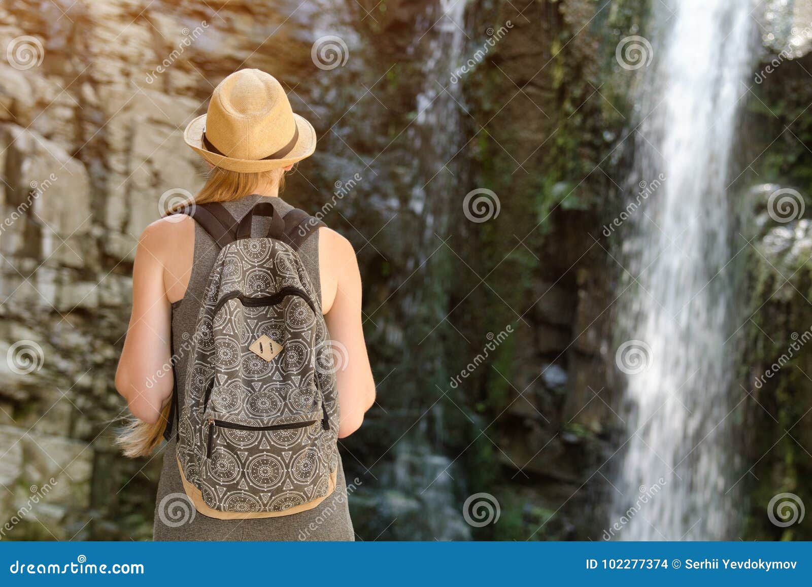 Girl with Backpack and in a Hat Looking at a Waterfall. View from the ...