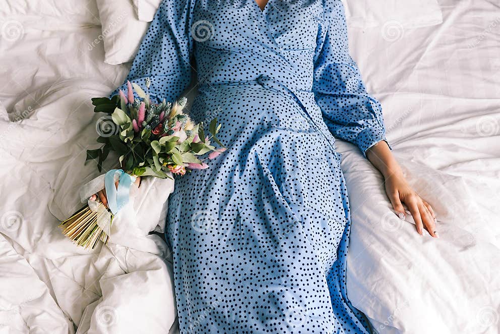 Girl In A Blue Dress And A Bouquet Of Flowers Is Lying On The Bed