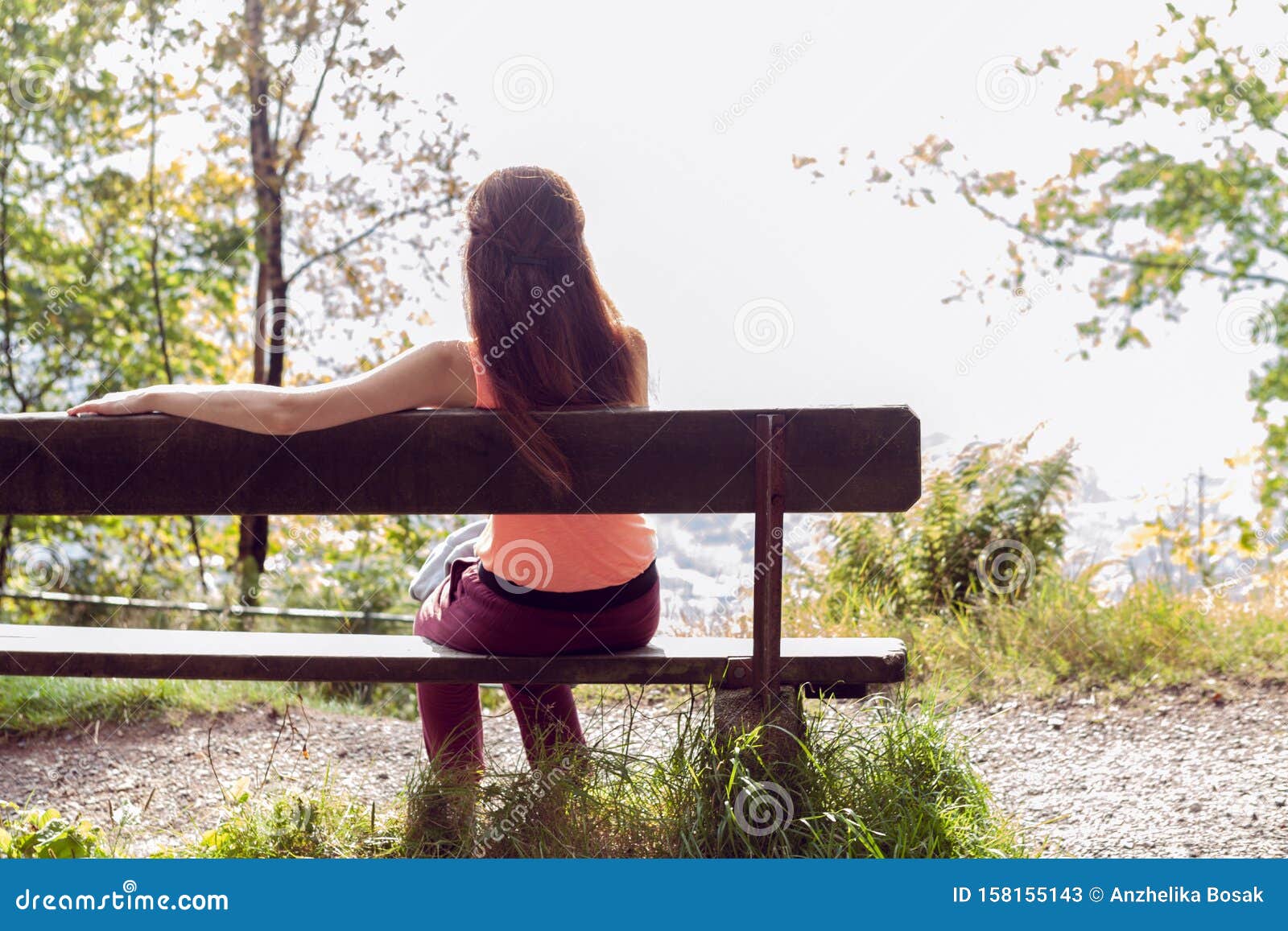 A Girl Sits on a Bench in the Forest, Her Back To the Camera Stock ...