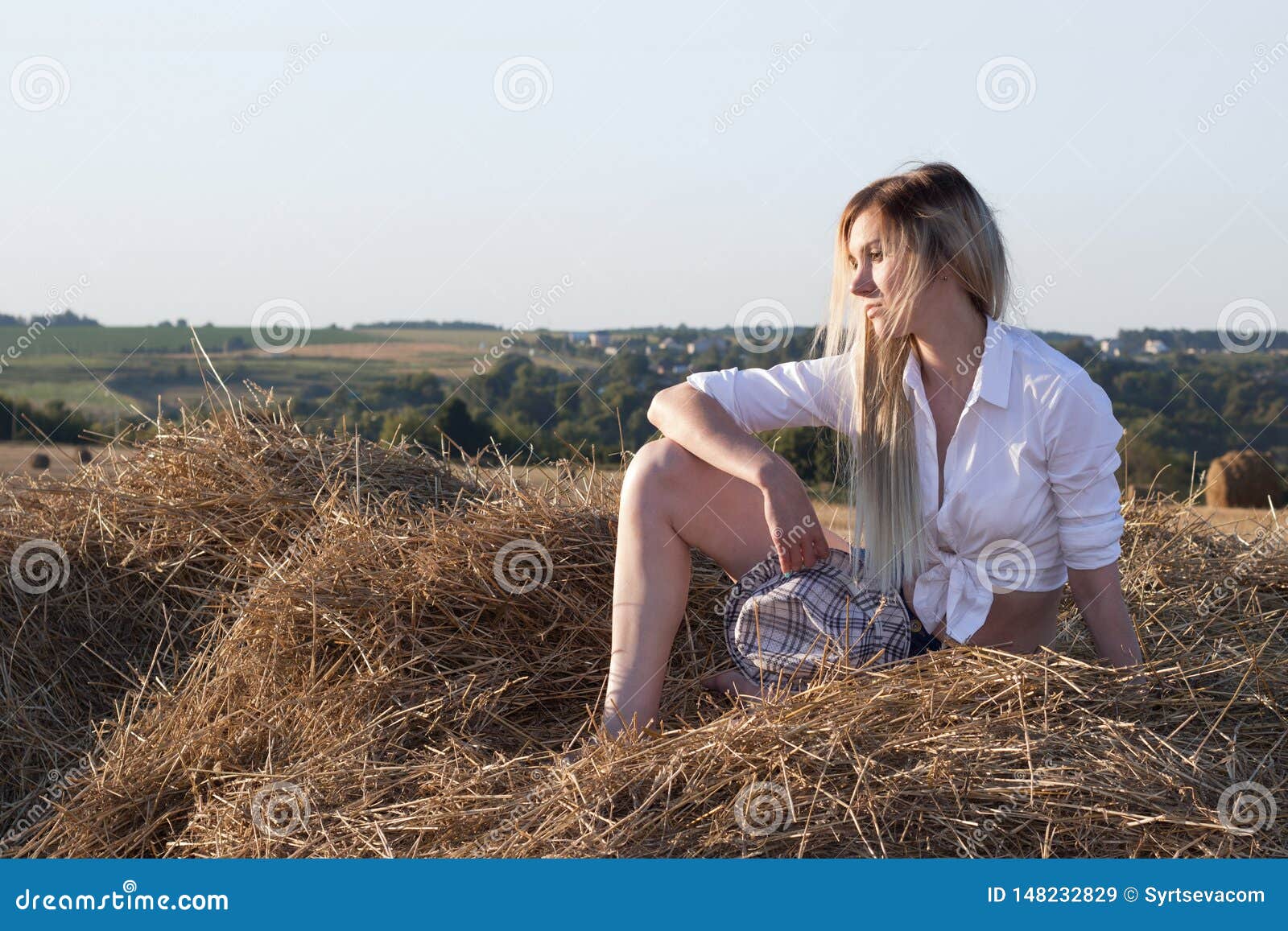 A Girl is Sitting in a Haystack on the Backdrop of the Rural Landscape ...