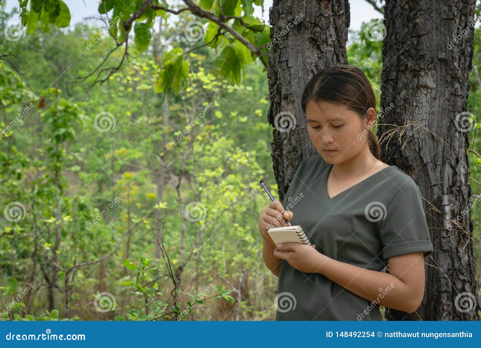 The Girl is Standing, Taking Notes in a Small Note Book in the Green ...