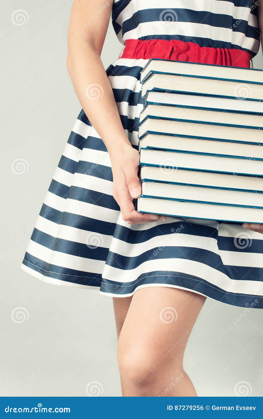 The Girl in a Striped Dress Holding a Stack of Books Stock Photo ...