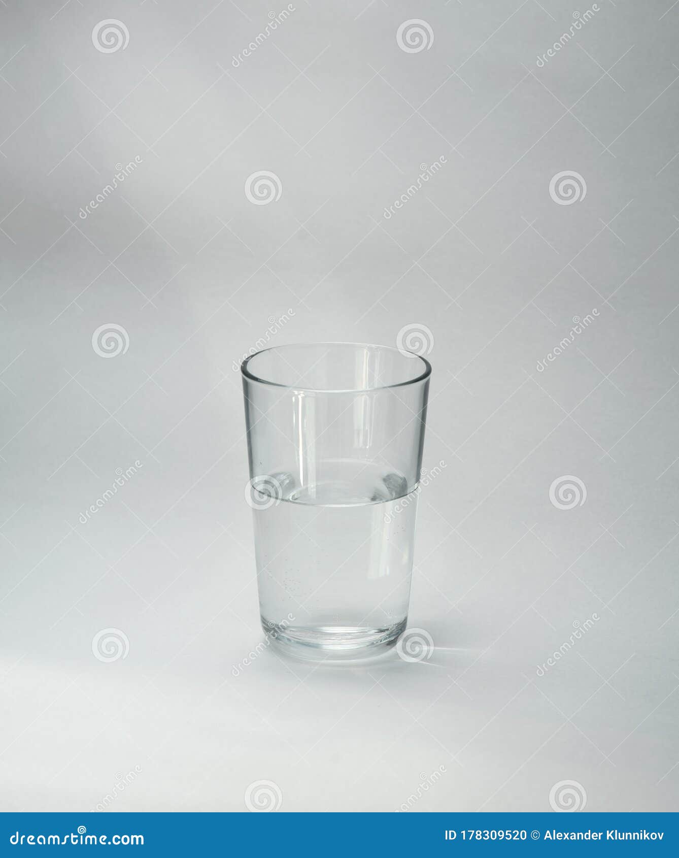 A Glass Cup Half Full of Water Stands on a Light Background. Close-up ...