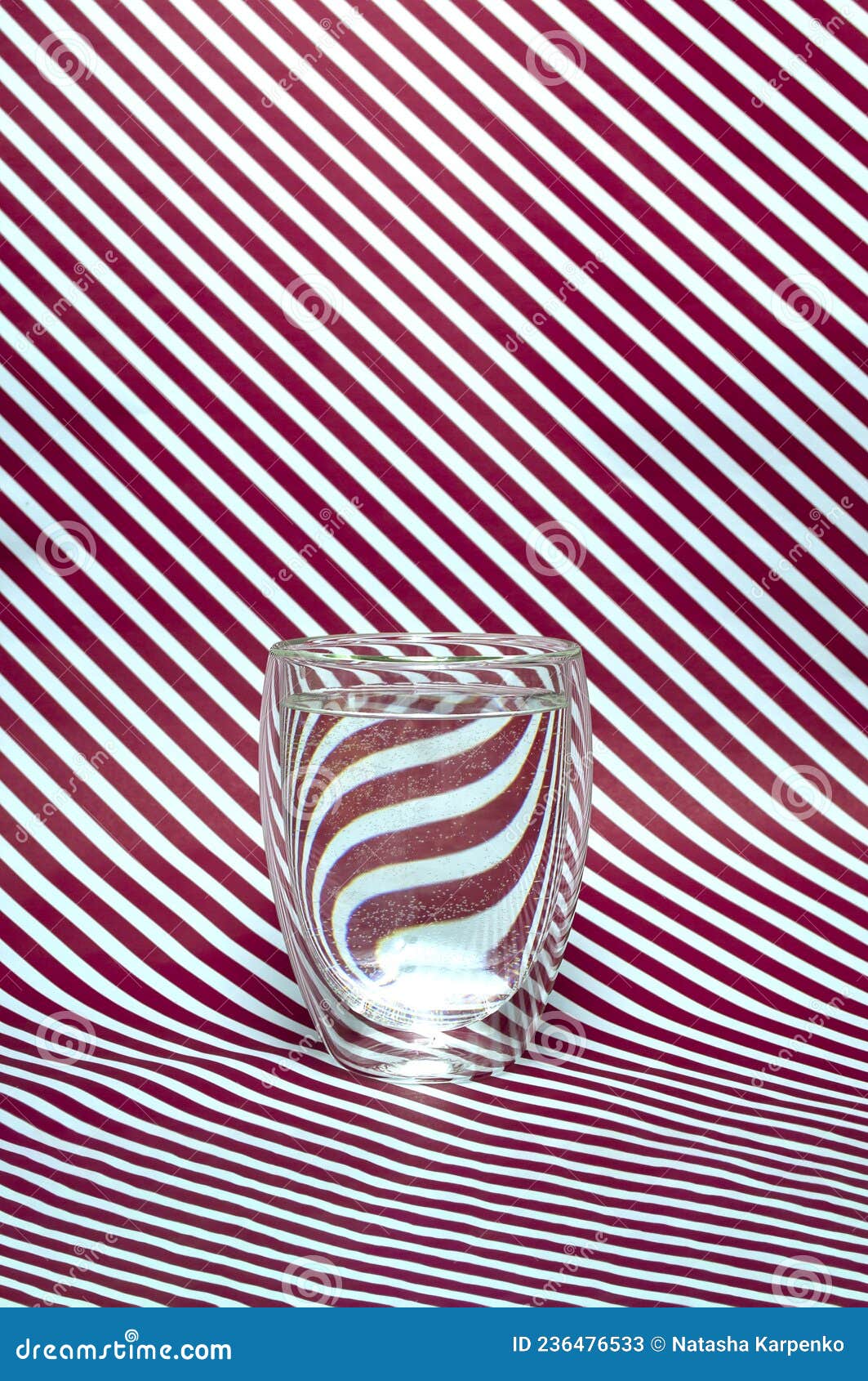 A Glass of Water with a Double Bottom on a Striped Background. Abstract ...
