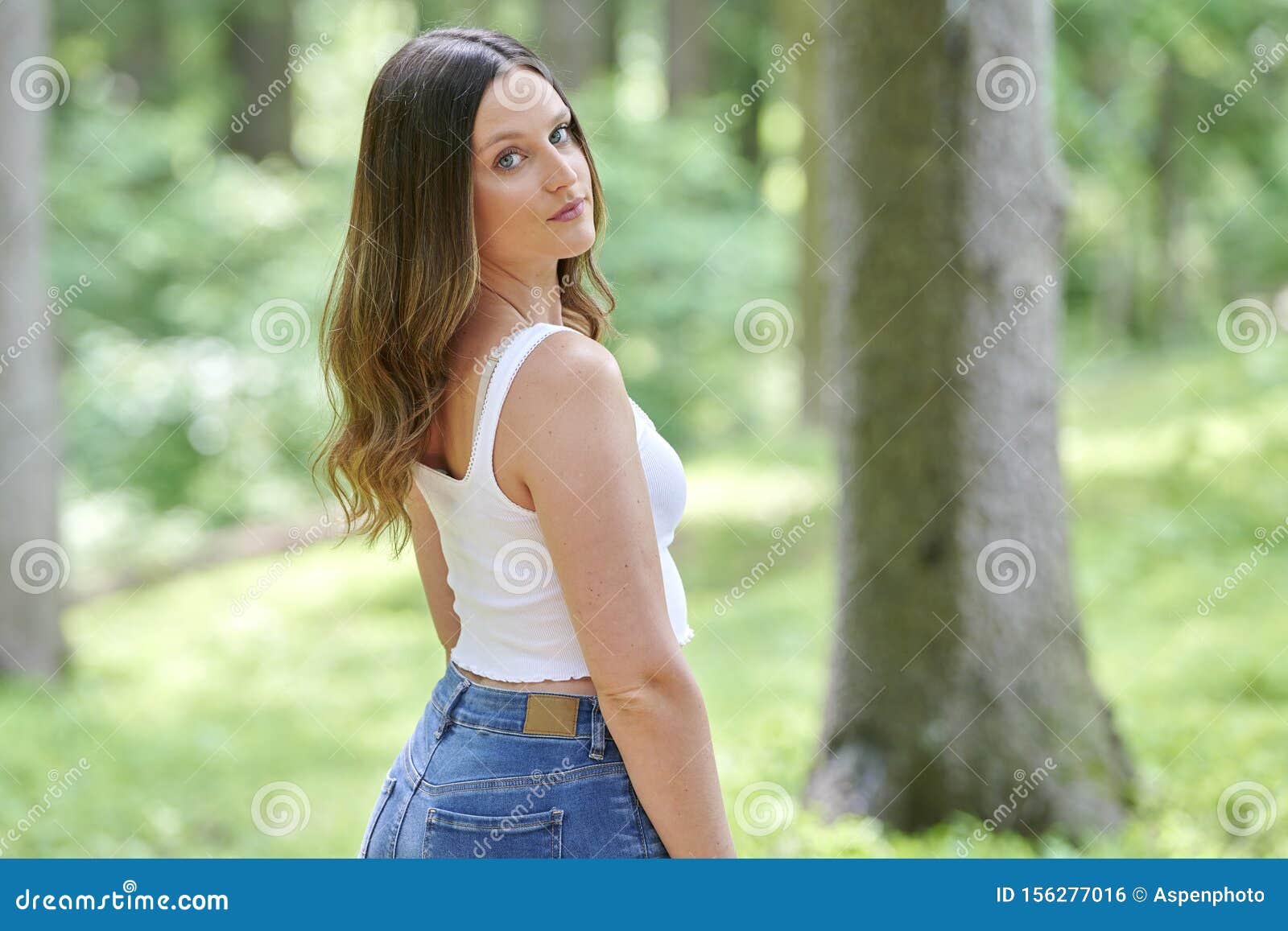 Gorgeous Young Woman In Blue Jeans And White Tank Top Poses Outside