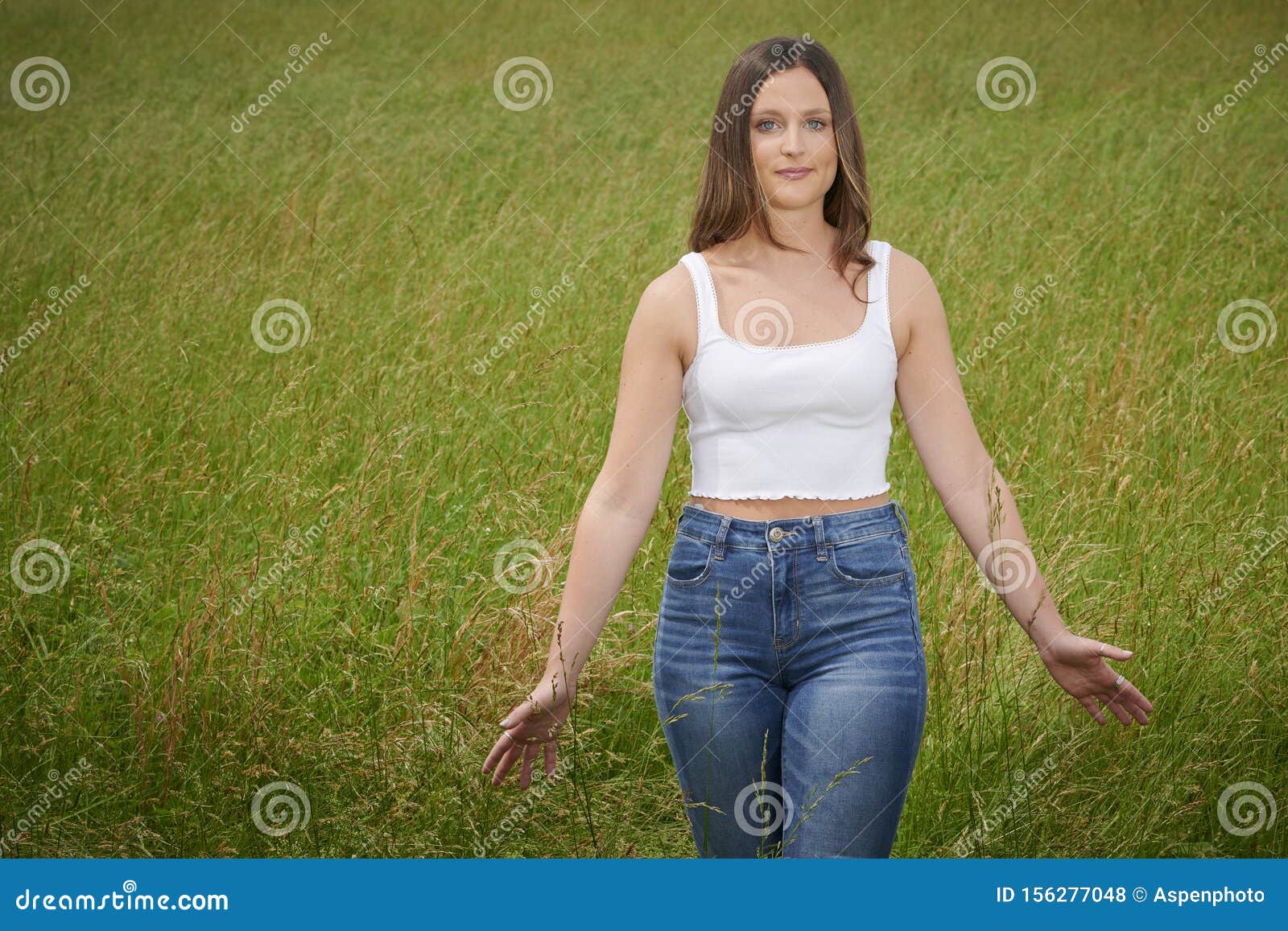 Gorgeous Young Woman In Blue Jeans And White Tank Top Poses Outside