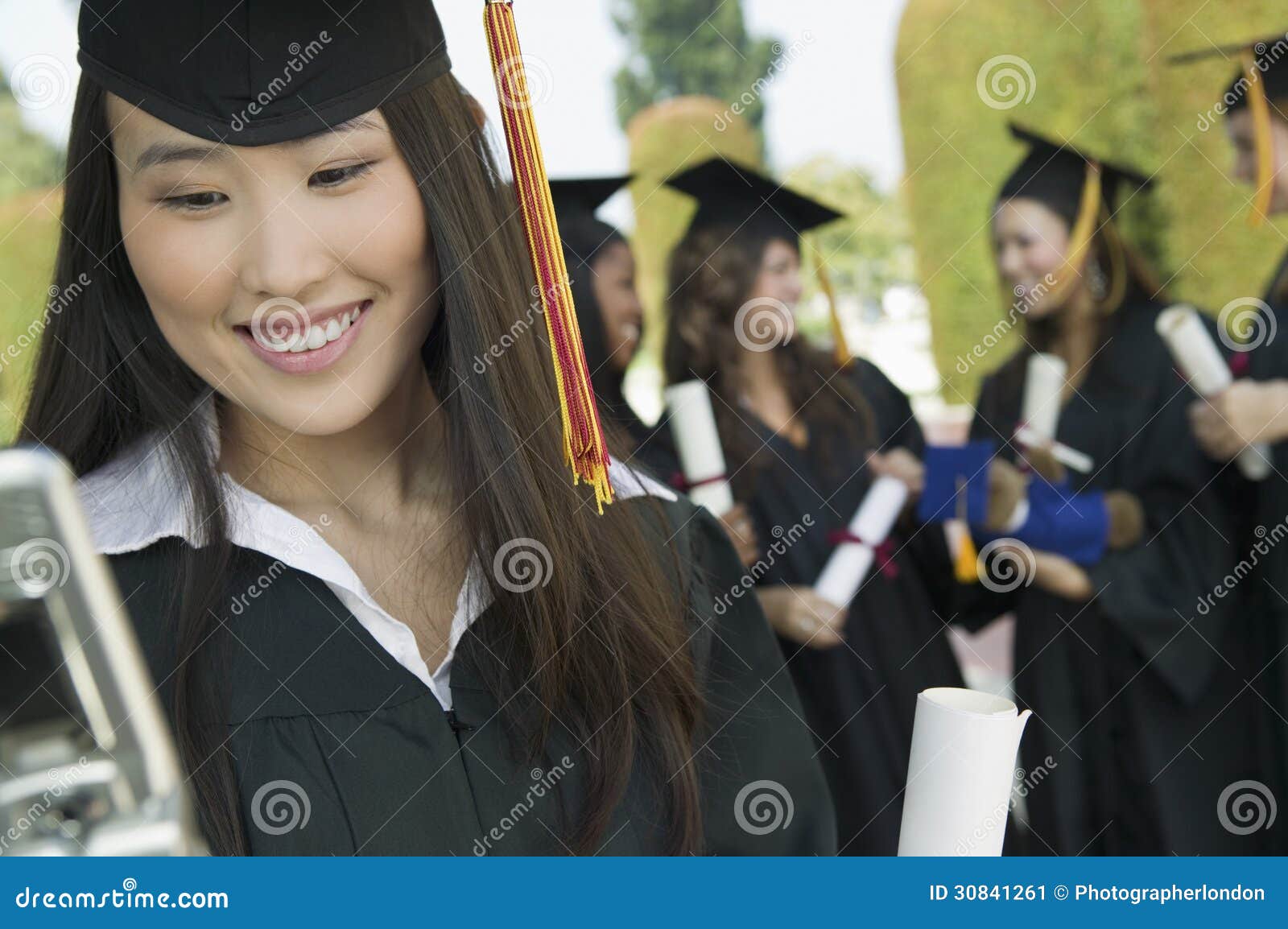 Graduate Using Cell Phone Outside with Others Behind Stock Image ...
